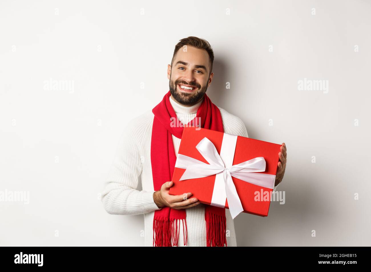 Christmas. Handsome young man holding gift and smiling, wishing happy ...