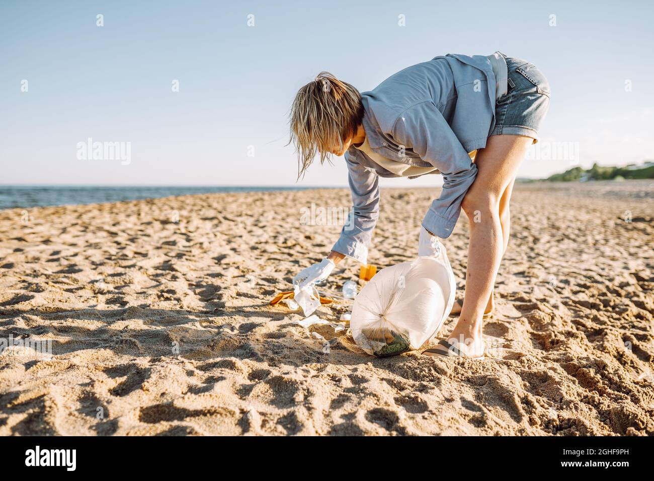 Woman pick up plastic garbage on sandy beach of the sea. Spilled ...