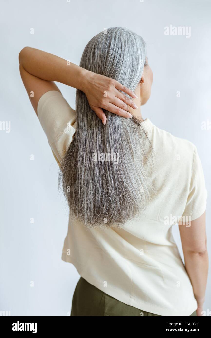 Middle aged woman adjusts long loose hoary hair on light grey ...