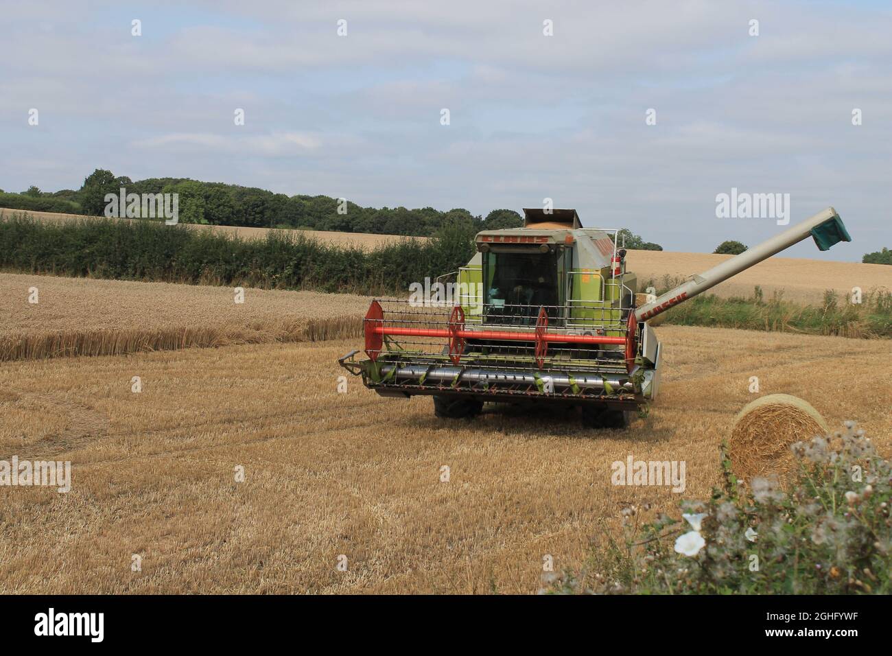 Combine harvester in a field waiting to harvest straw with hay bale in ...