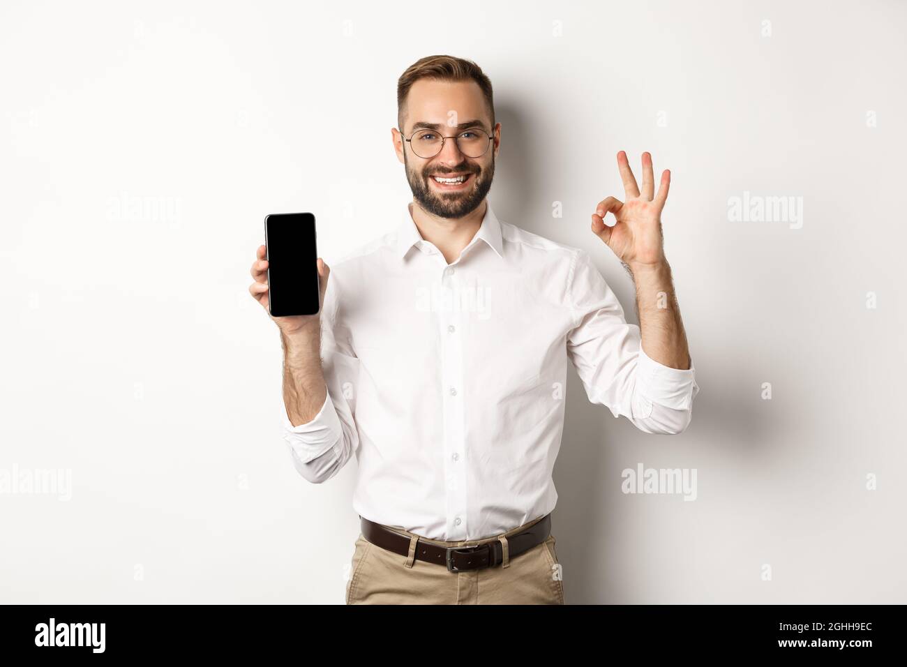 Satisfied young manager showing smartphone screen and okay sign ...