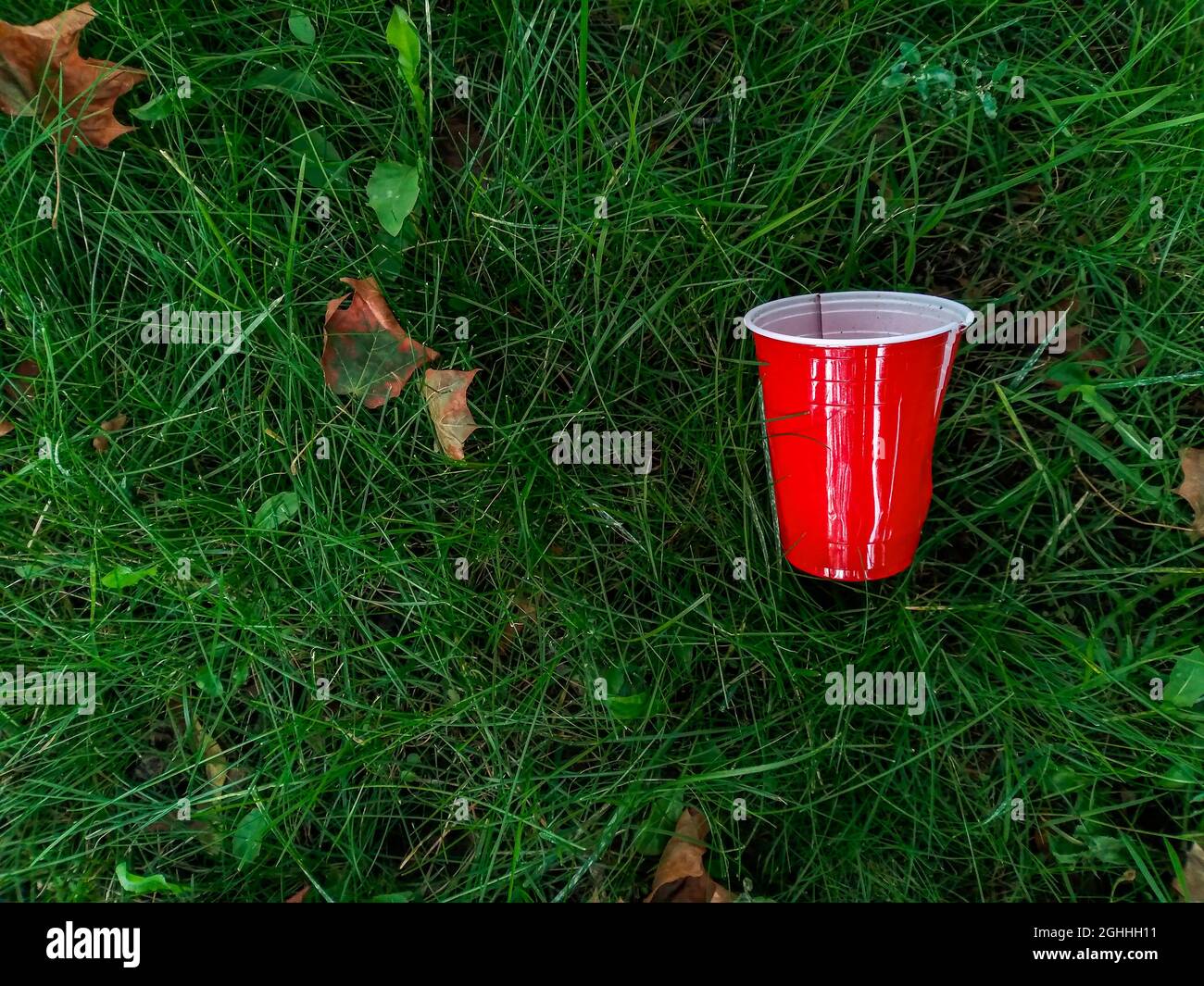 Used red plastic water coffee tea cup thrown on a grass lawn - symbol ...