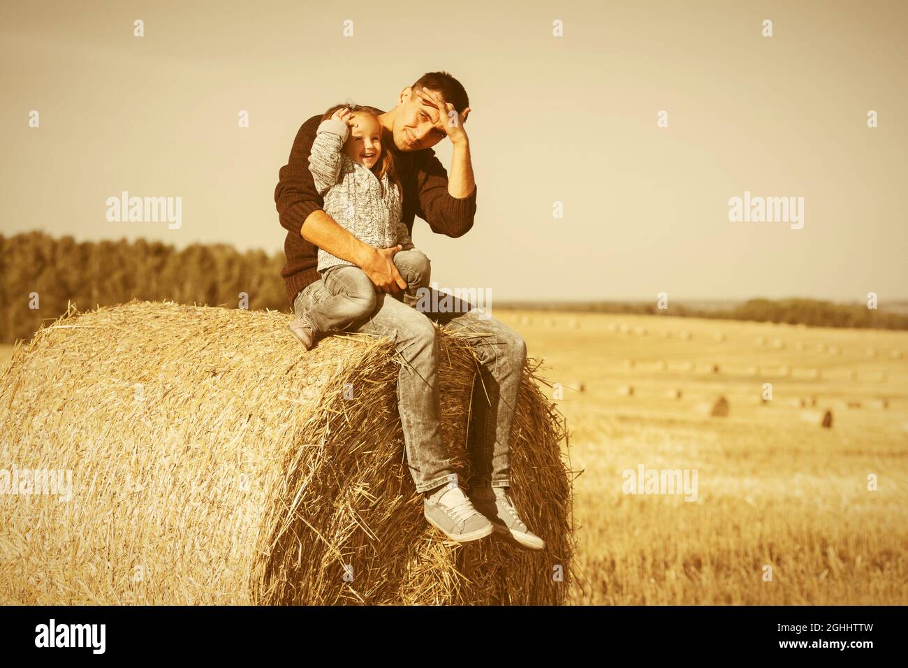 Happy father and two year old girl sitting on hay bale in harvested ...