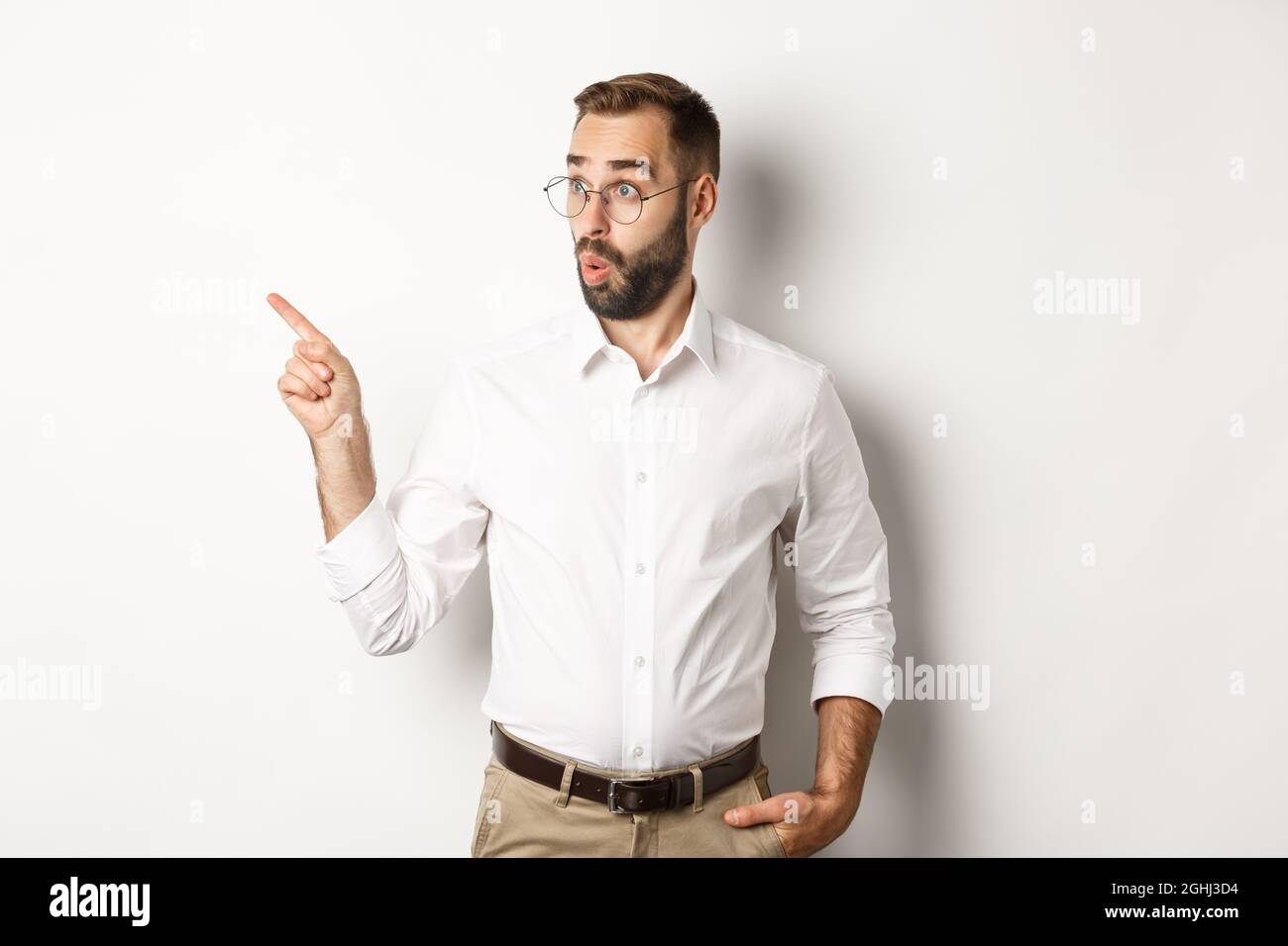Intrigued young man in glasses pointing finger left, looking at promo ...