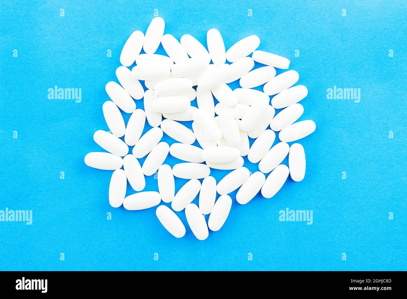 Full frame white oval pills texture on blue paper background. Medicinal ...