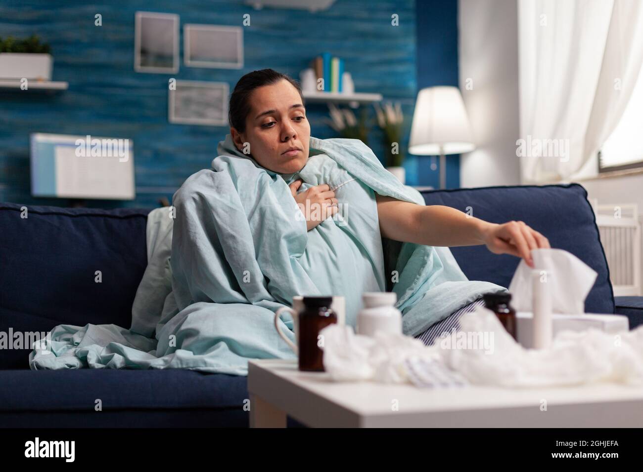 Woman with flu symptoms sitiing at home ill on couch suffering. Young caucasian person using ...