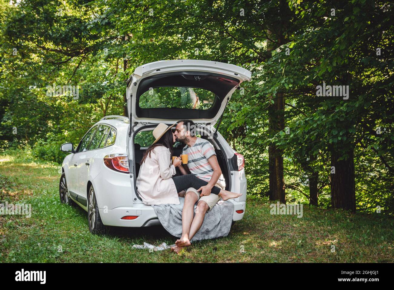 Happy Young Couple On A Camping Road Trip Sitting In Car Boot Kissing