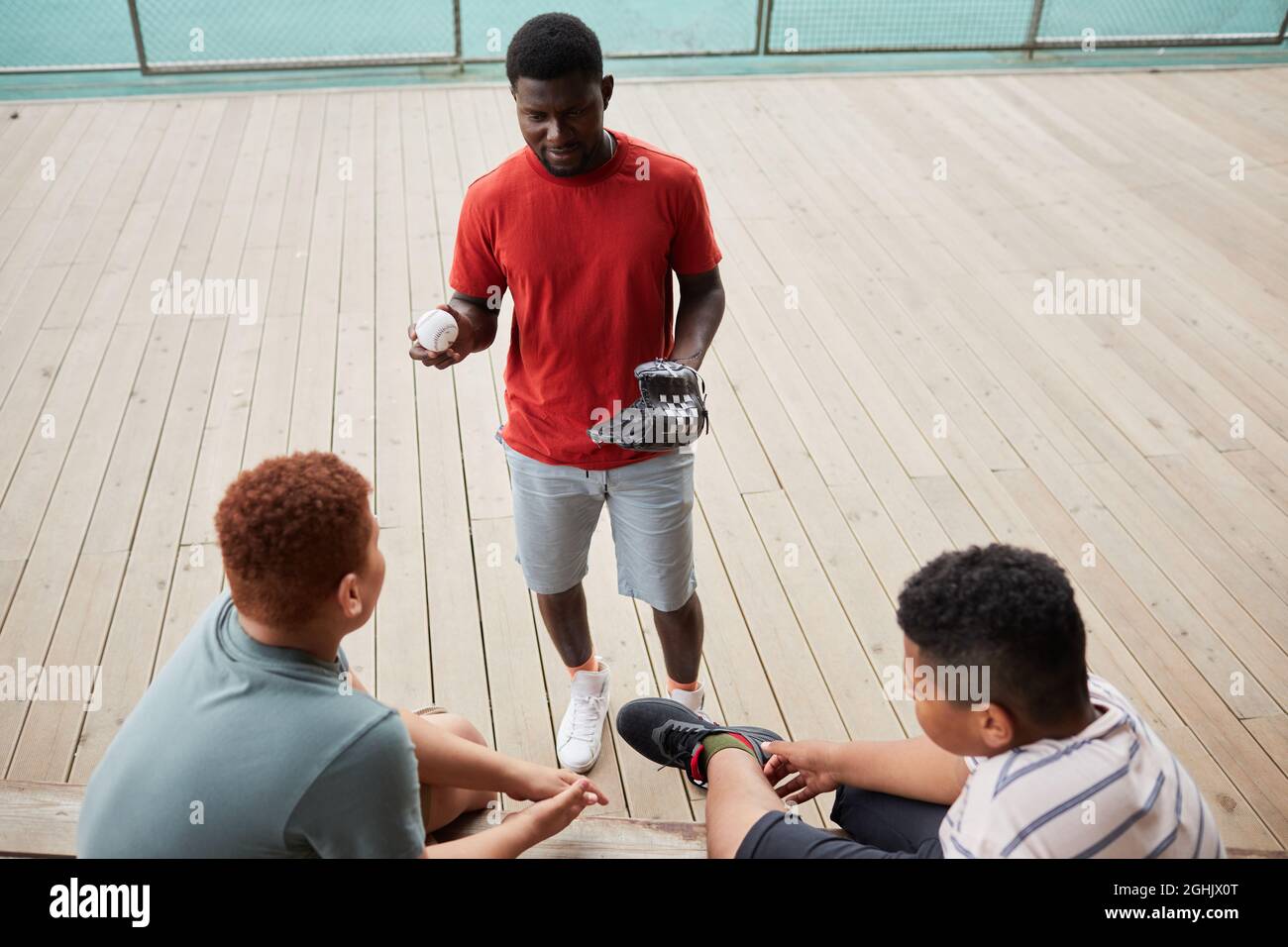 Young African-American coach in orange tshirt holding ball and baseball ...