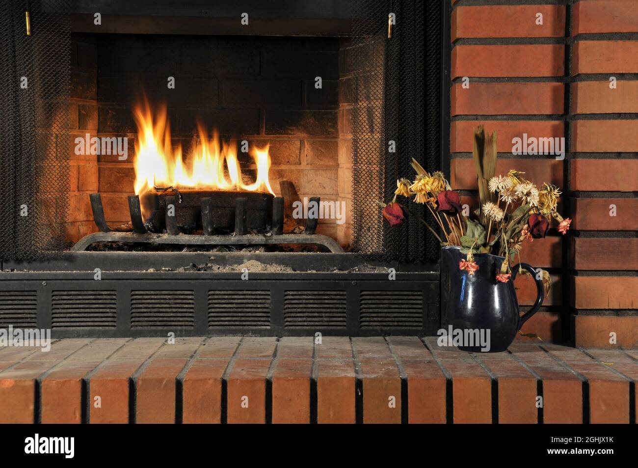 Fire burning with artificial log in fireplace with brick and pitcher of ...