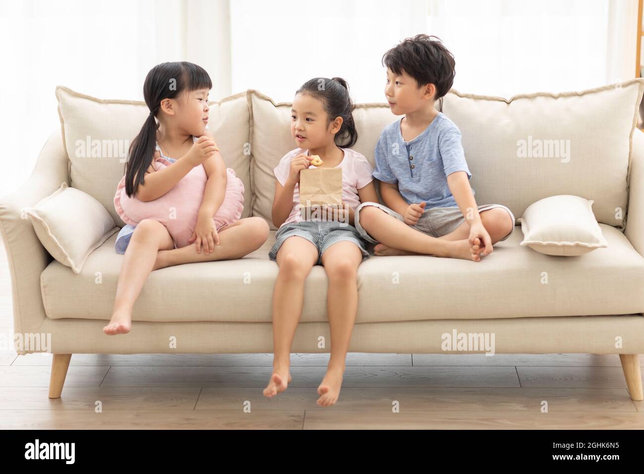 Cute children eating biscuits on sofa Stock Photo - Alamy