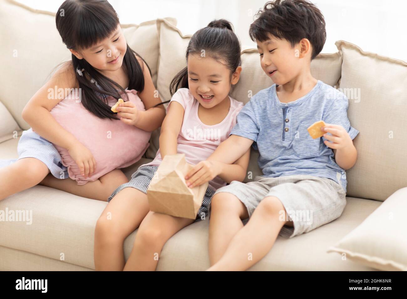 Cute children eating biscuits on sofa Stock Photo - Alamy