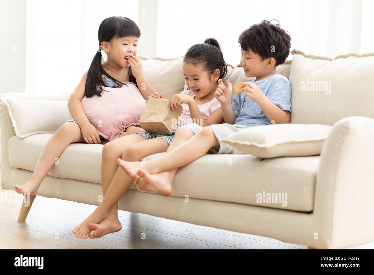 Cute children eating biscuits on sofa Stock Photo - Alamy