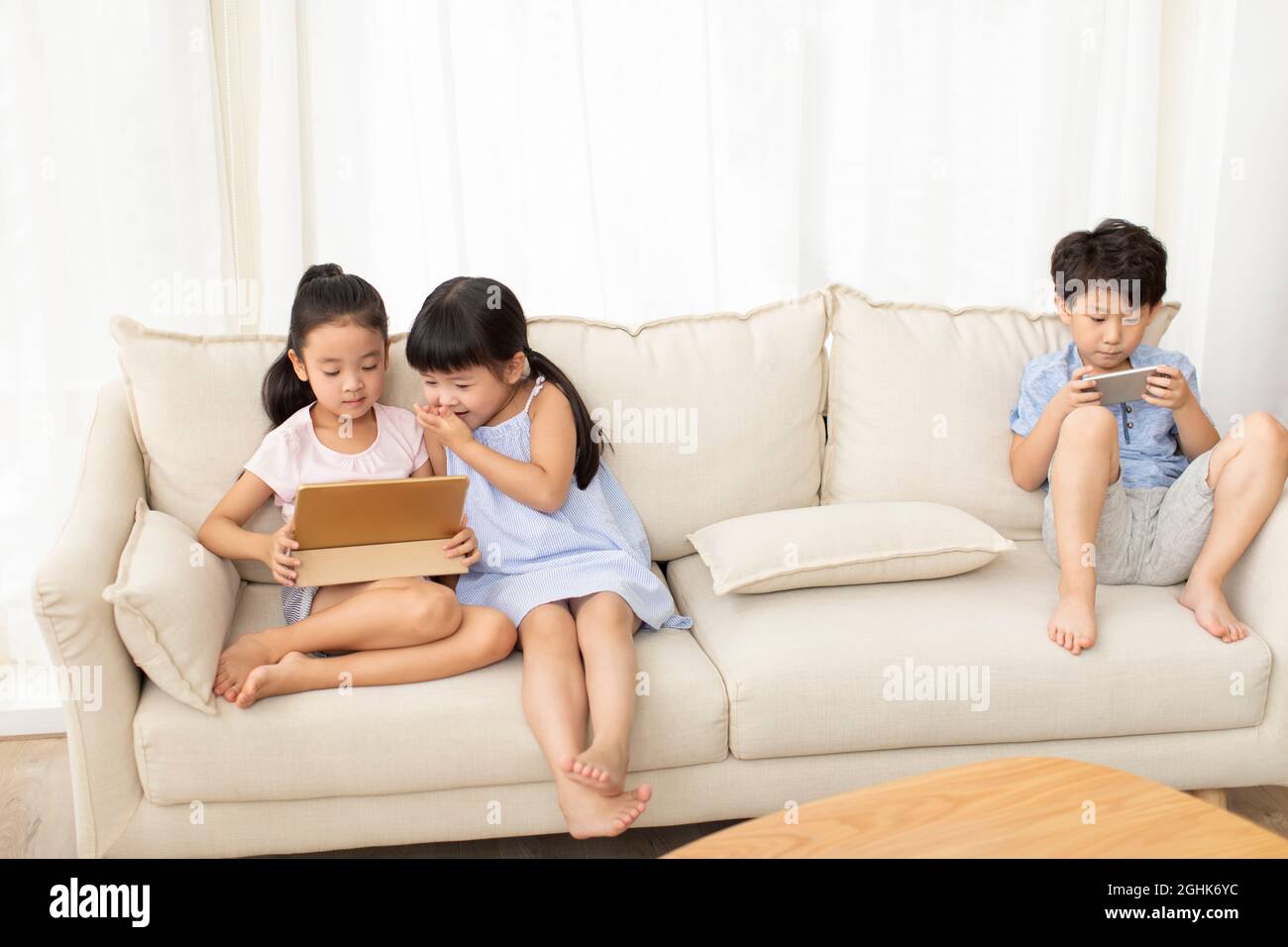 Cute children using digital devices on sofa Stock Photo - Alamy