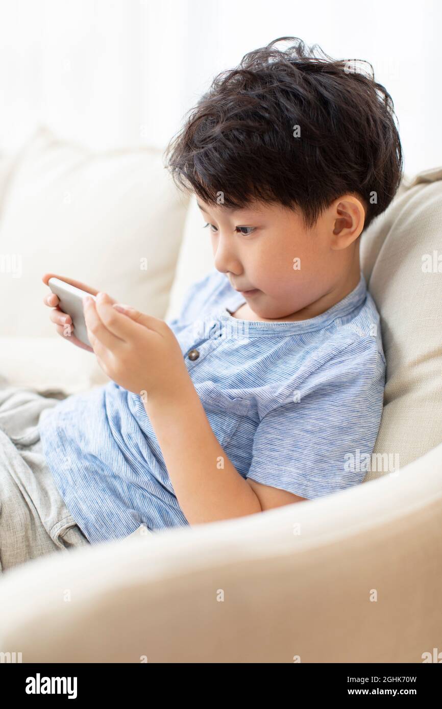 Cute little boy using smart phone on sofa Stock Photo - Alamy