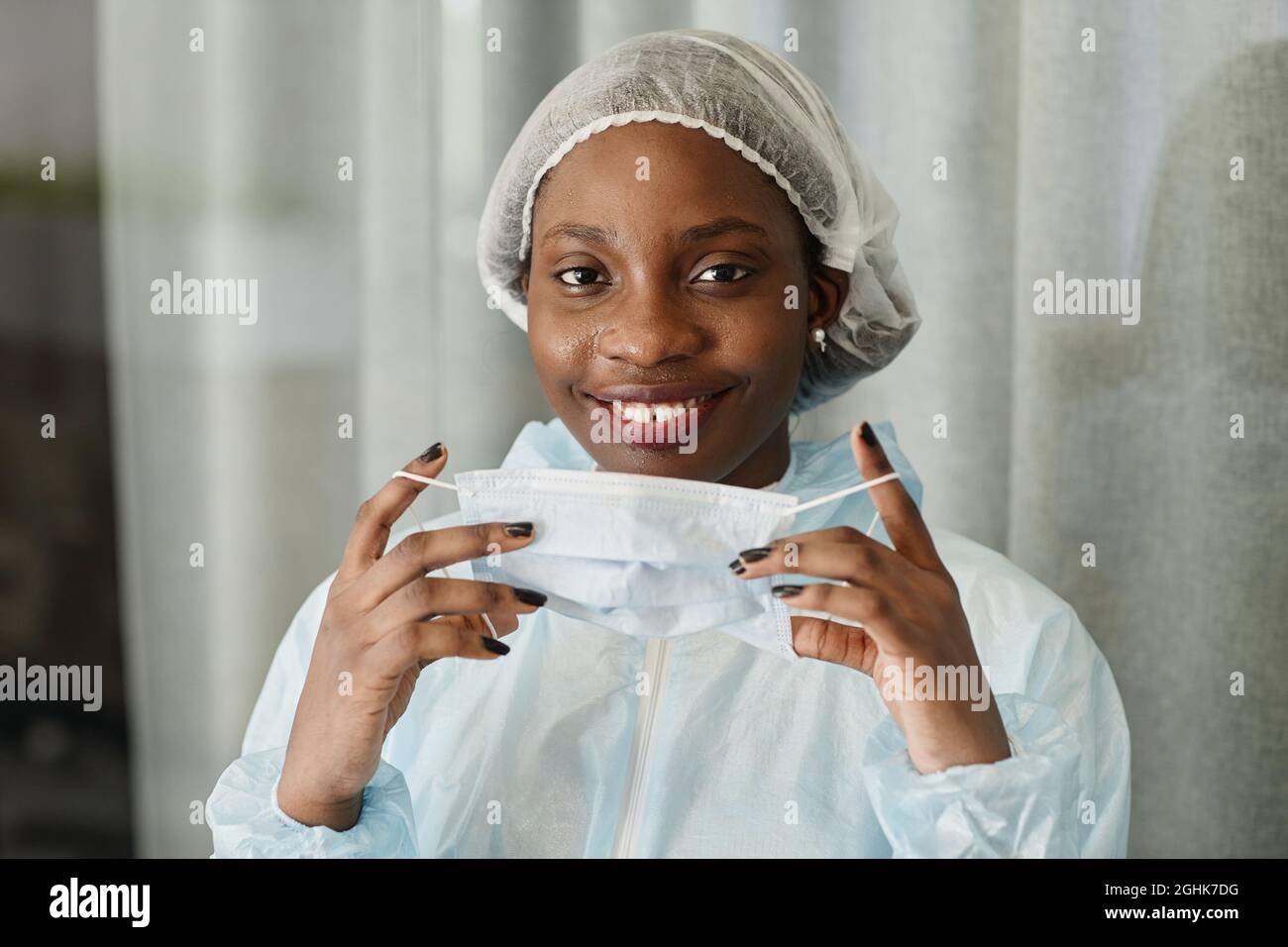 Face of pretty smiling young Black nurse taking off medical mask from ...