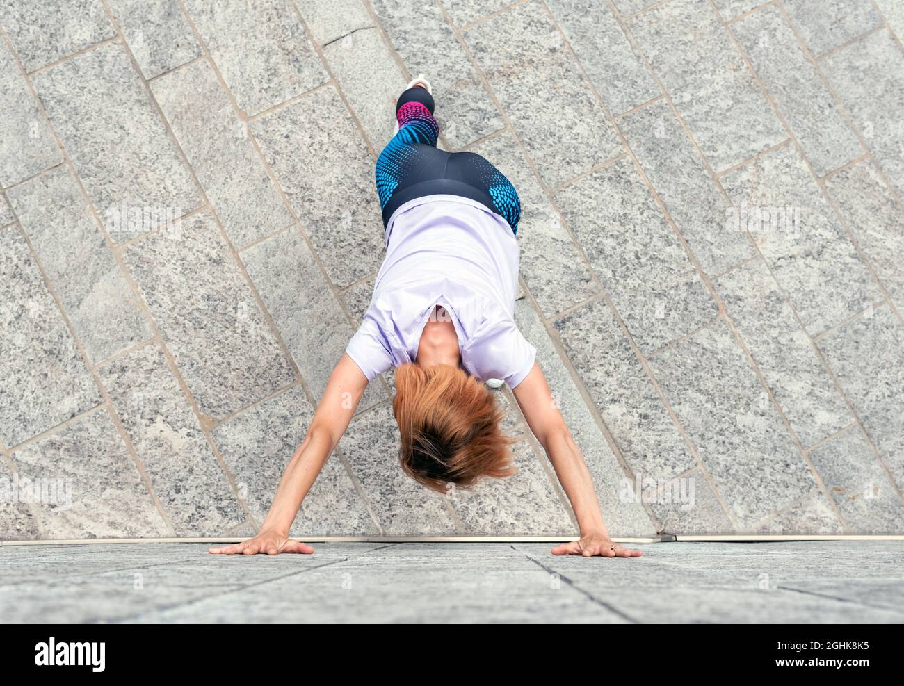 Athletic woman doing stretching exercises on a sidewalk in town in a ...