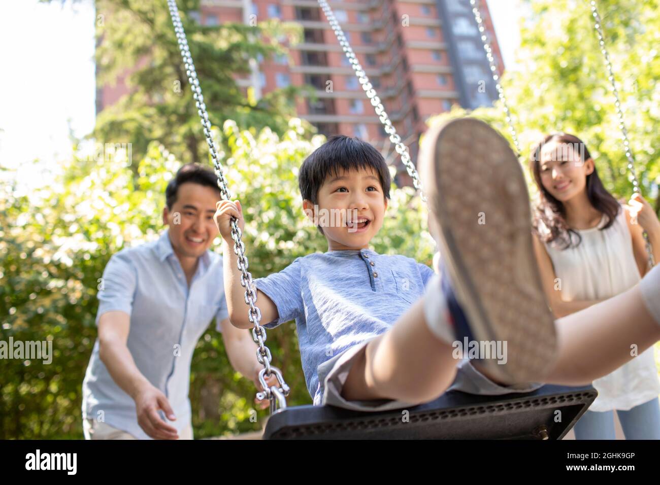 Happy young parents pushing son on swing Stock Photo - Alamy