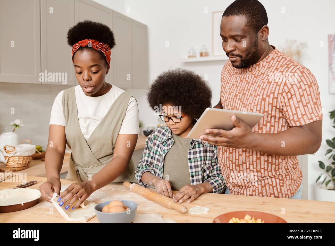 Young African family of three cooking homemade pastry by kitchen table ...