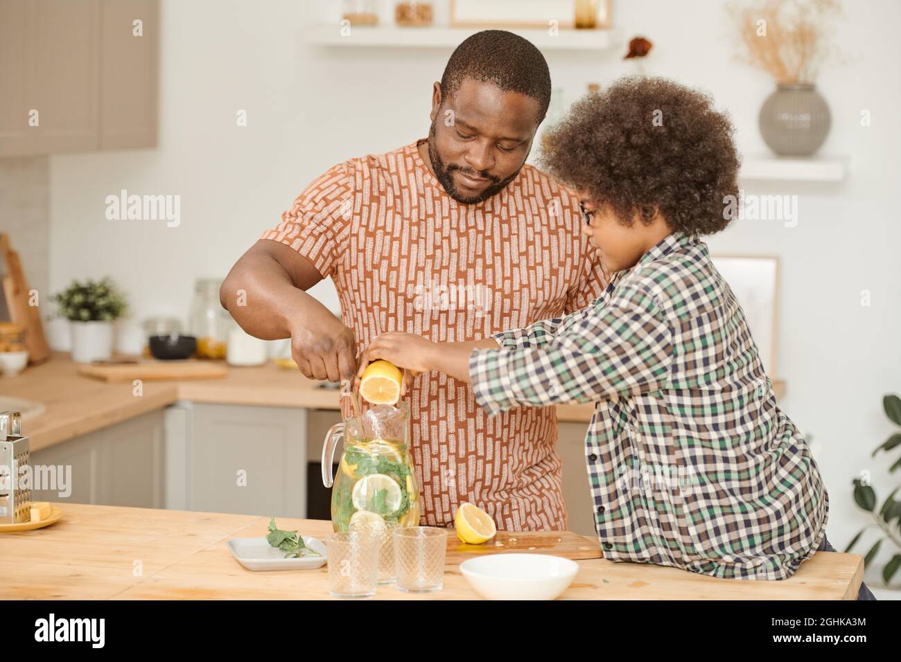 Cute little boy squeezing lemon juice into jug with lemonade while ...