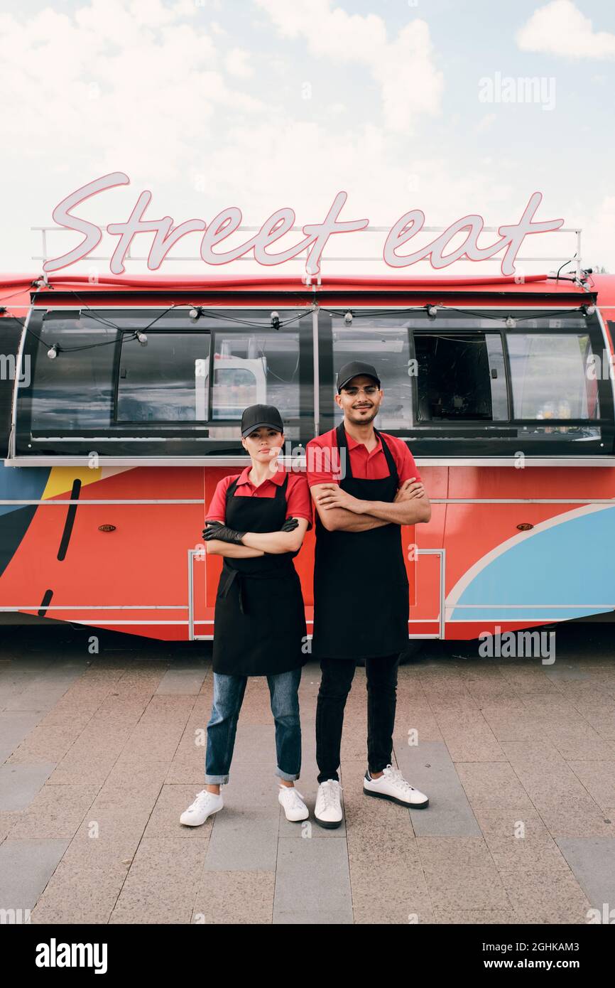 Two young successful workers of food truck standing against red van ...