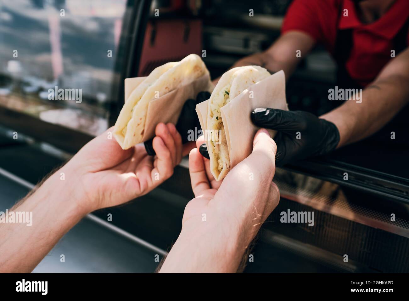 Hands of young man taking tasty snacks wrapped into paper held by ...