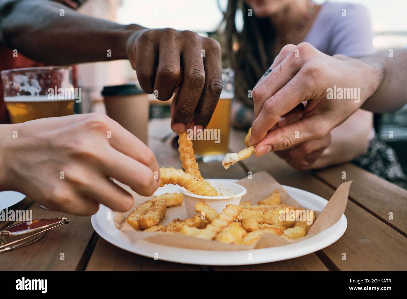 Hands of intercultural hungry friends putting french fries into sauce ...