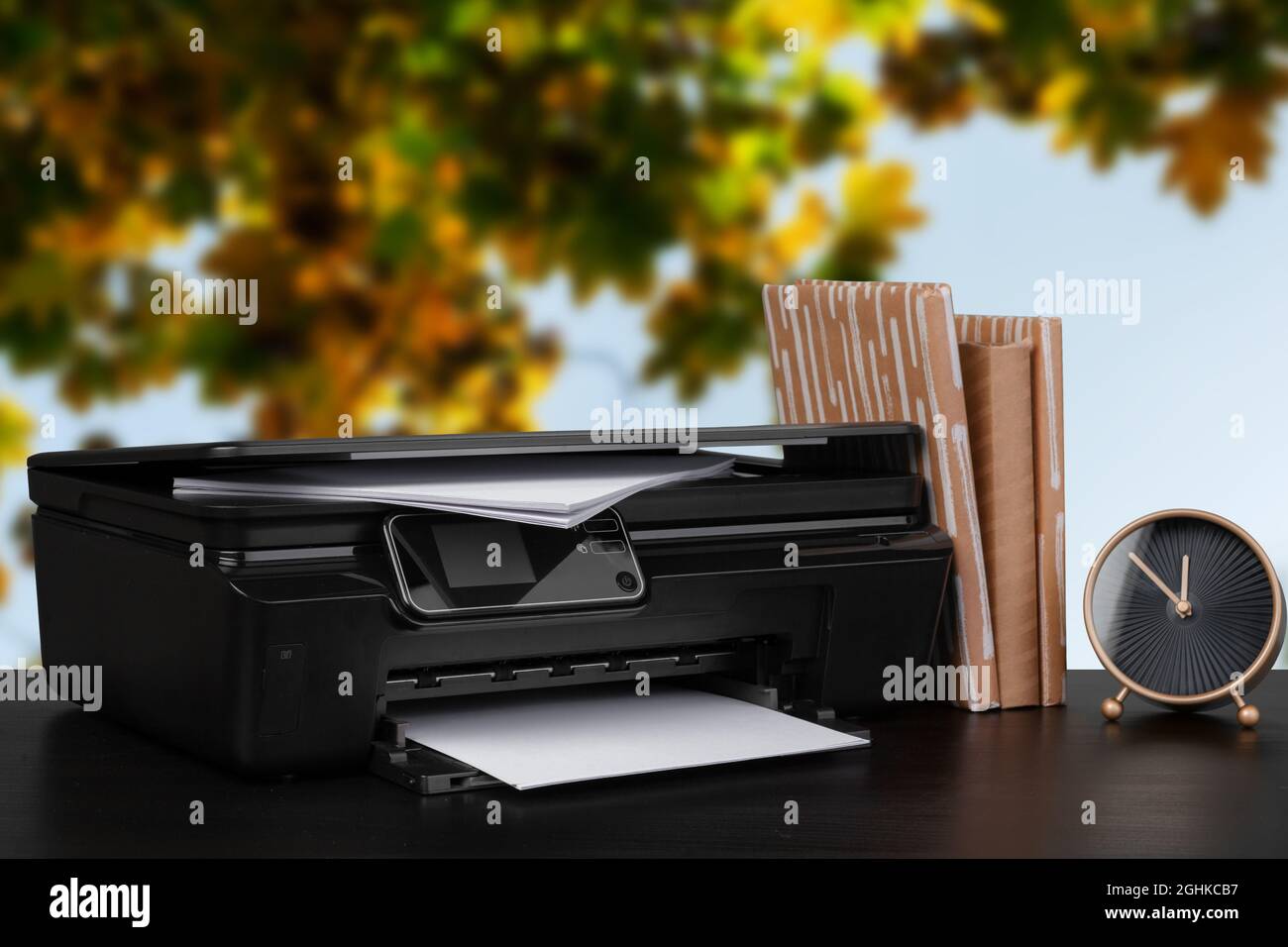 Compact home printer on desk with books against blurred background ...