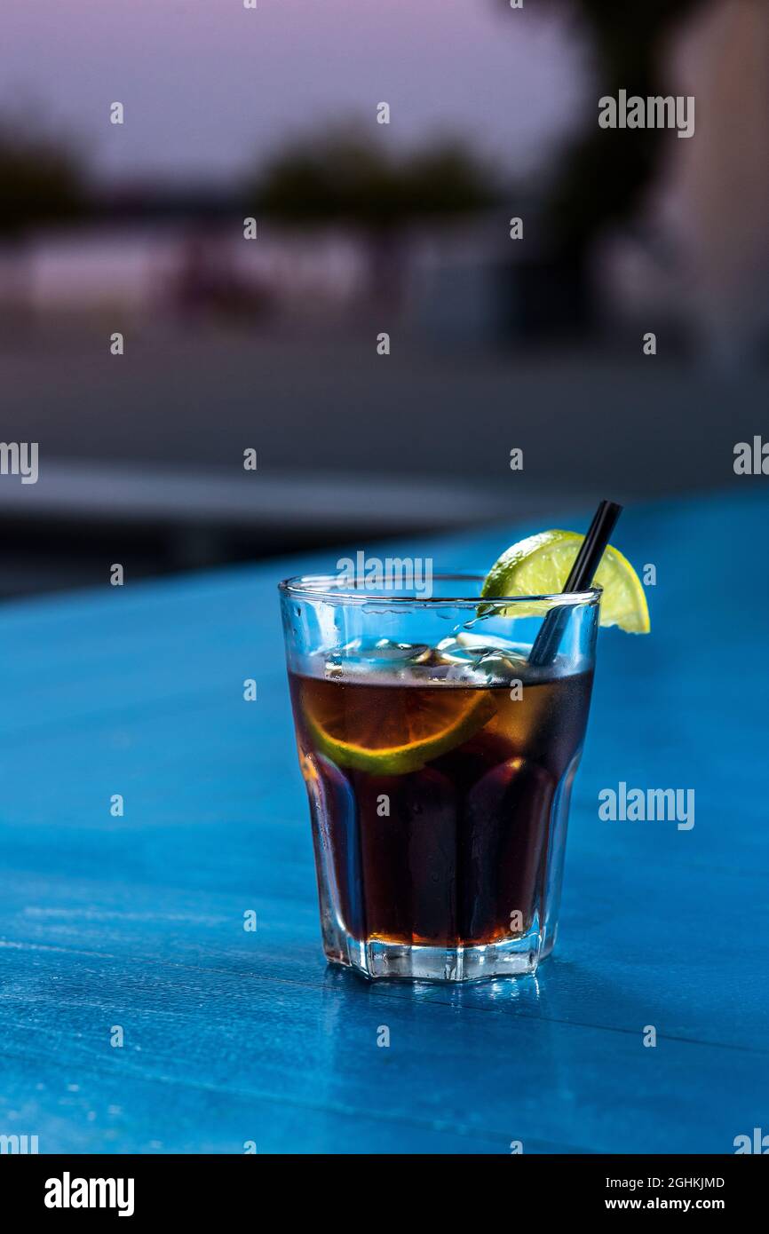Rum cola casual cocktail with ice cubes and lime at summer bar stand ...