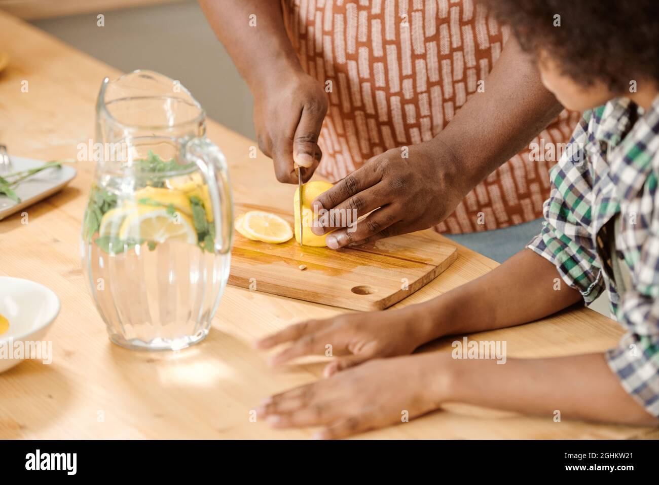 Little boy standing by his father slicing fresh lemon while making ...