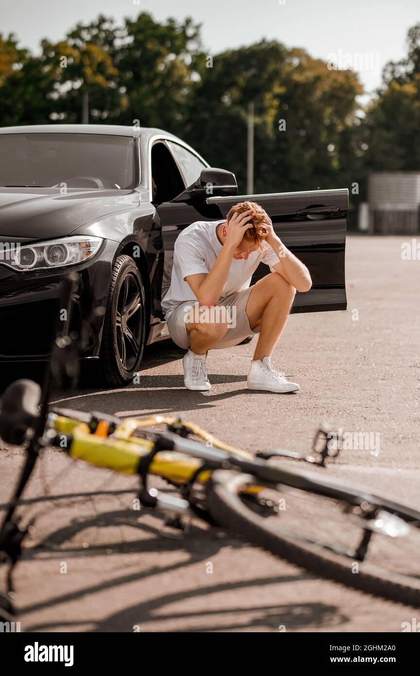 Desperate guy crouched near car after accident Stock Photo - Alamy