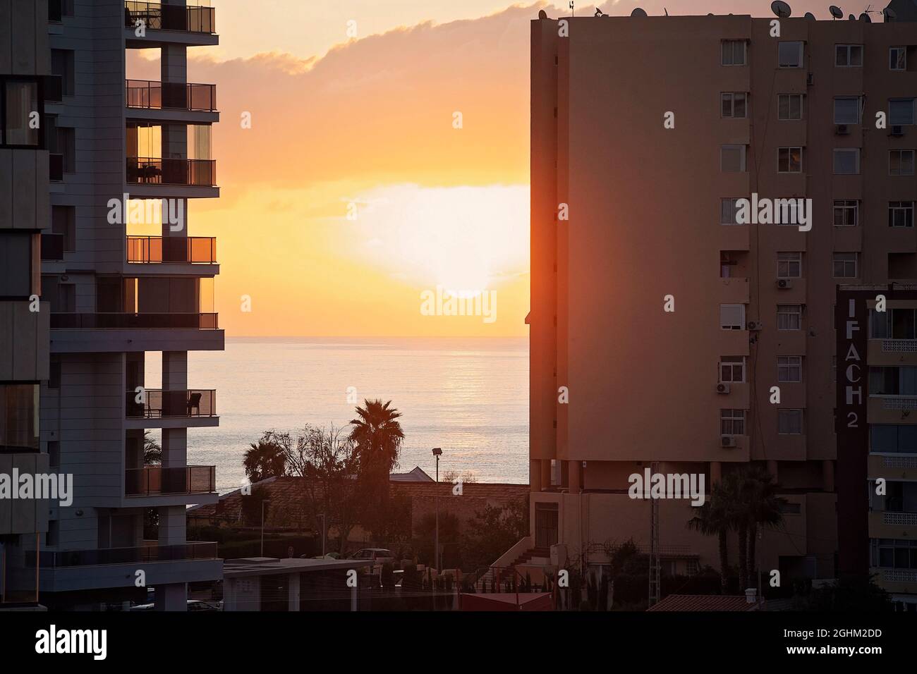 The Sunset in Spain with an ocean view with buildings and some palm ...