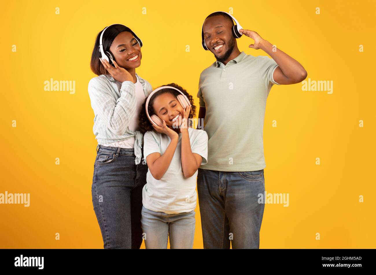 Happy black parents and their daughter enjoying music in headphones ...