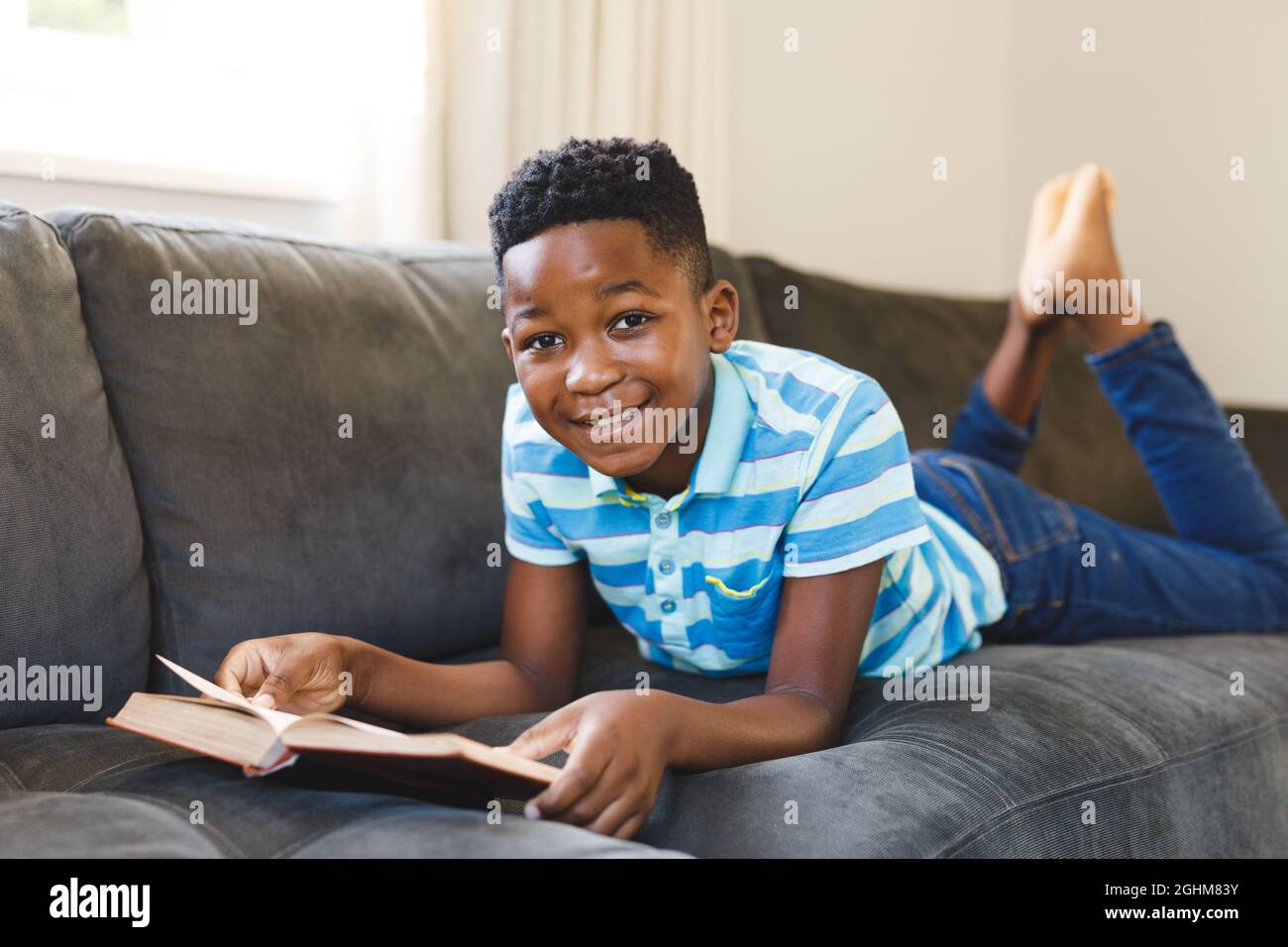 Portrait of smiling african american boy reading book and lying on ...