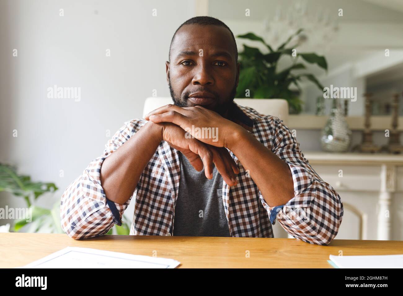 Serious african american man sitting at table in dining room, listening ...