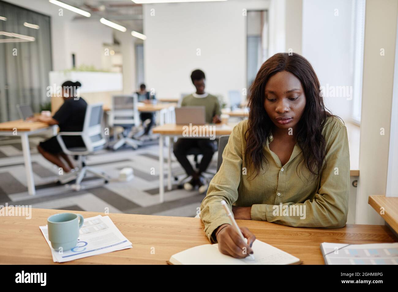 Pretty serious buisness lady sitting at office desk with cup of coffee ...