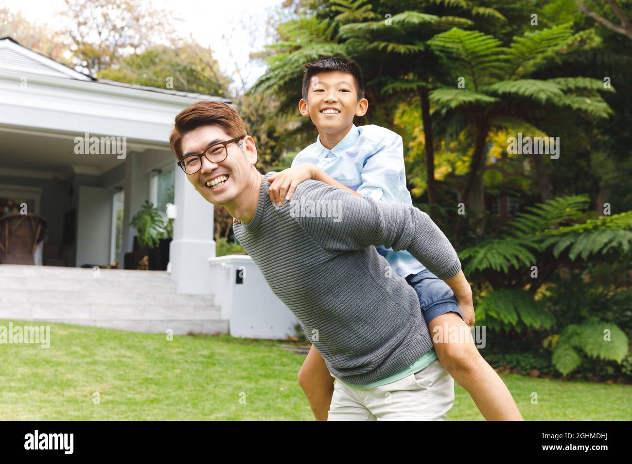 Portrait of happy asian father carrying his son and smiling outdoors in ...