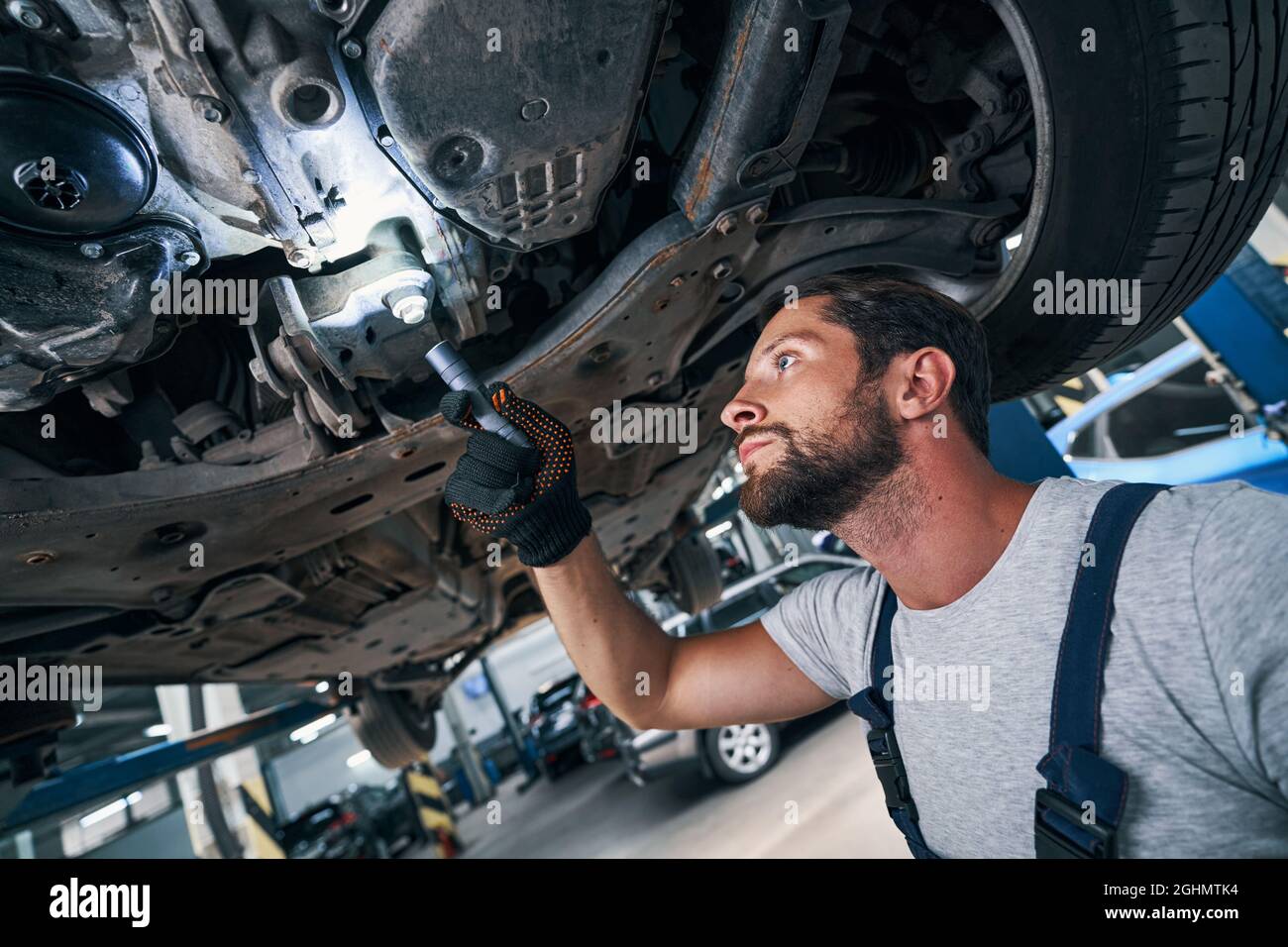 Automobile repairman examining car underside using flashlight Stock ...