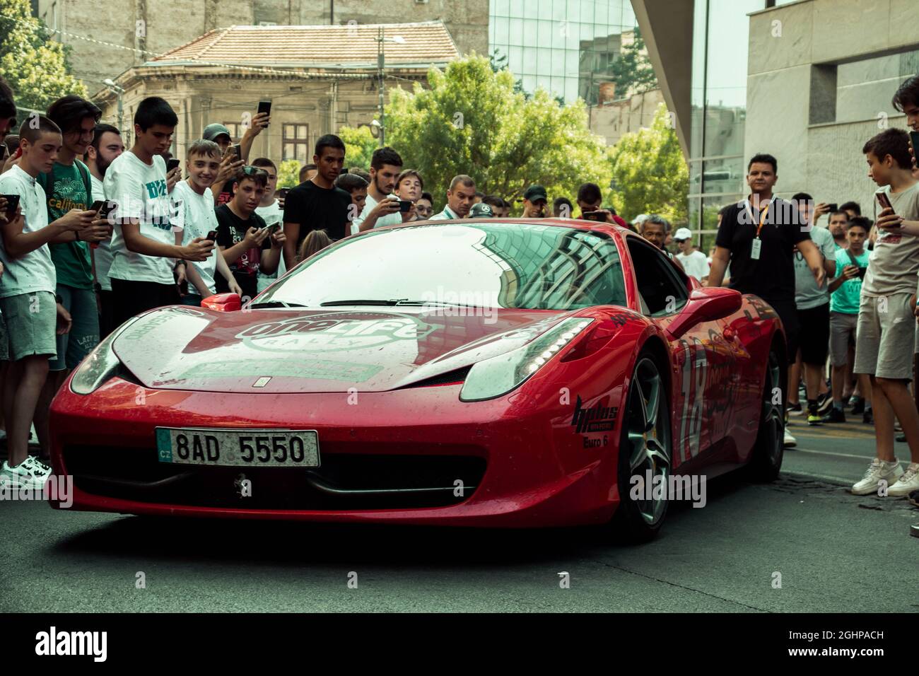 Red Ferrari 458 parking on a street with a cheerful crowd of people ...