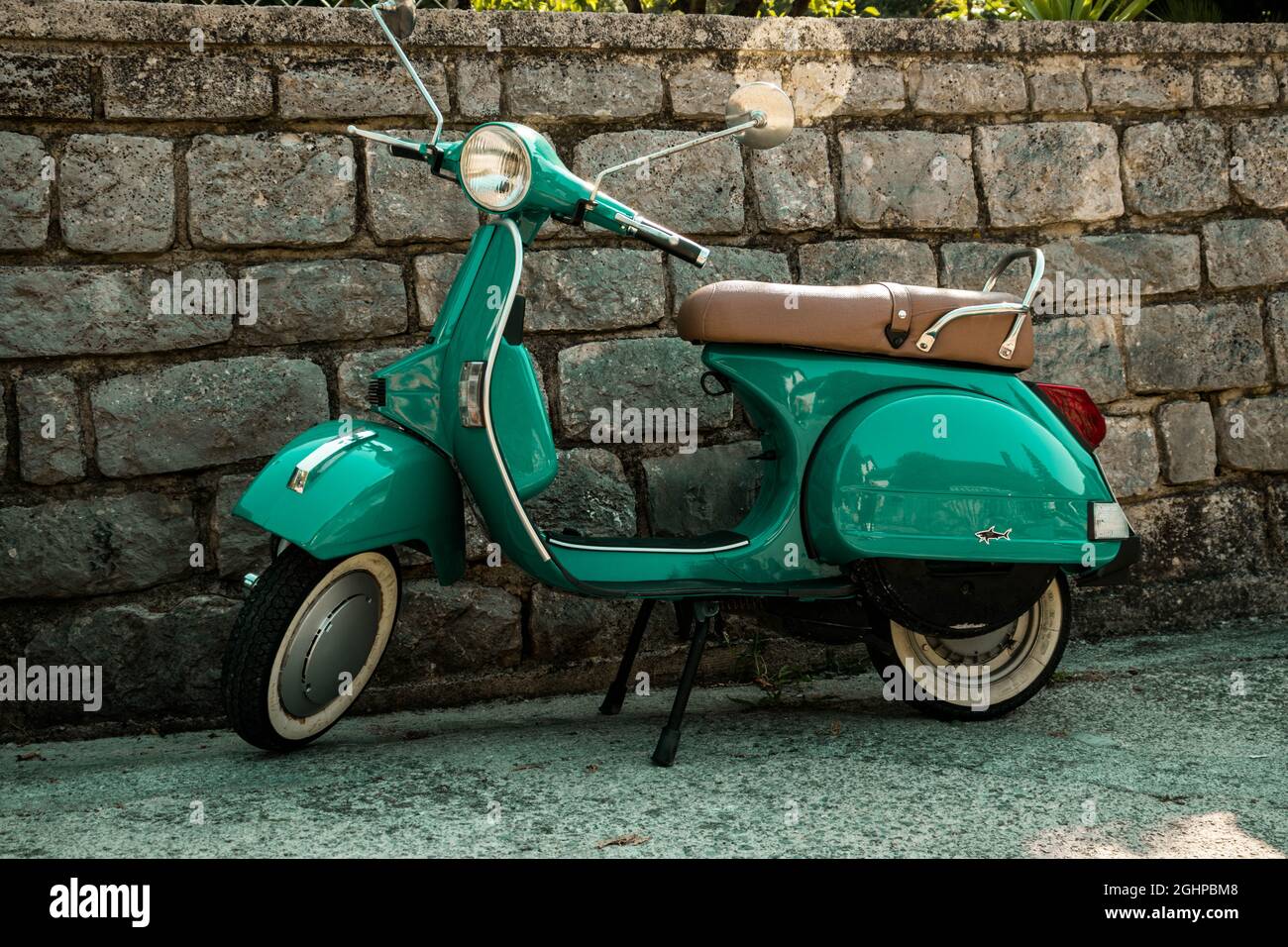 Light blue mopped parked on a street next to a cobblestone wall with ...