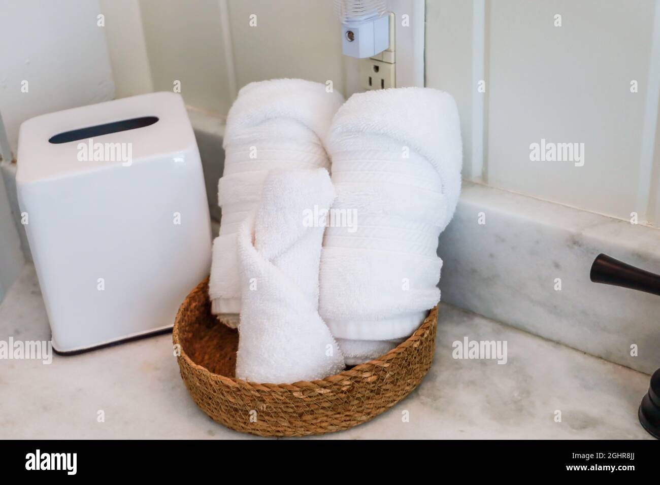 A basket of organized clean rolled white towels on a bathroom counter ...