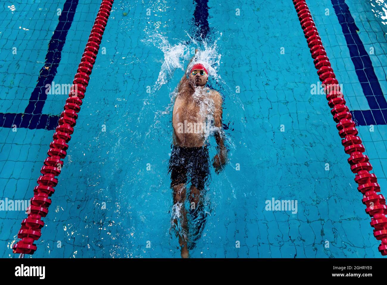 Young professional male swimmer in red cap and goggles practicing and ...