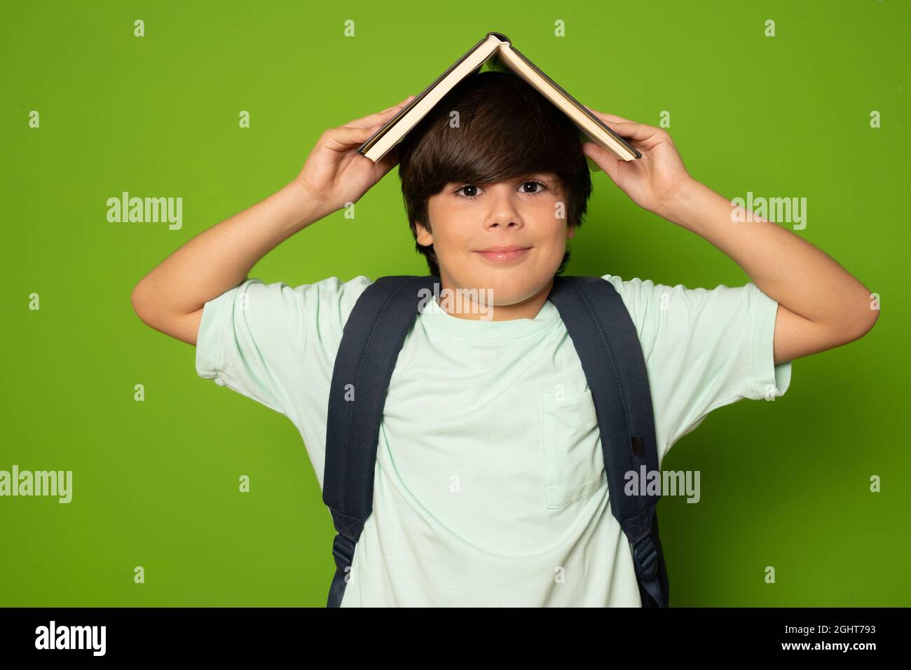 portrait of student with book on the head against a green background ...