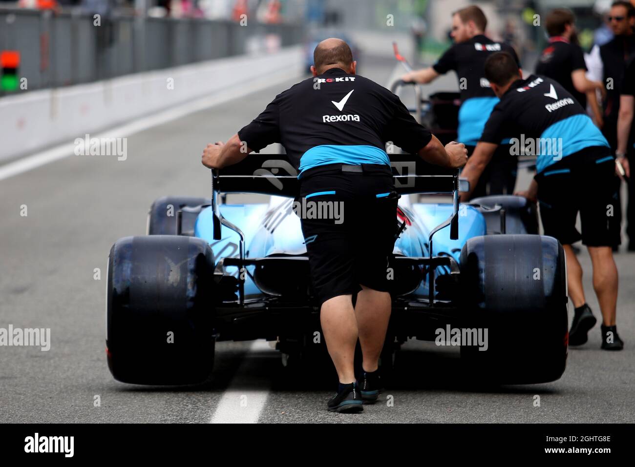 Williams Racing mechanics pus a Williams Racing FW42 down the pit lane ...