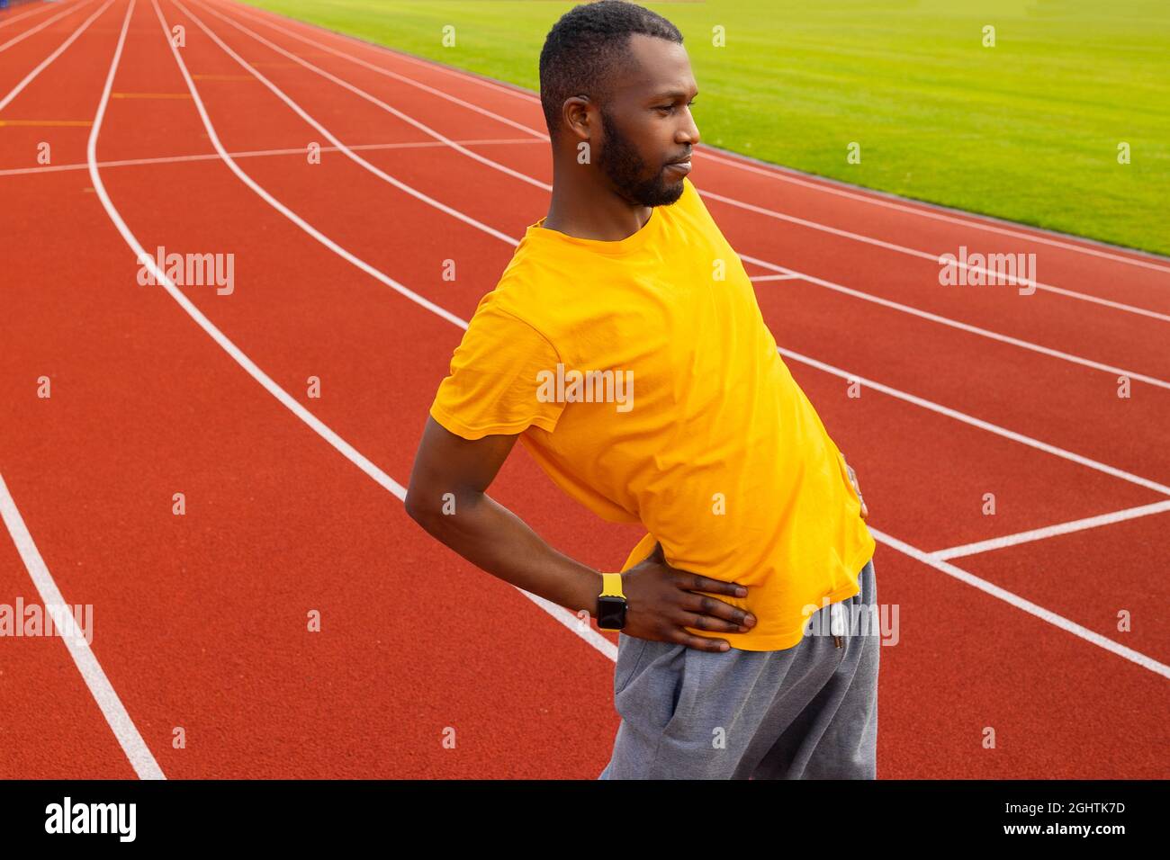 Sportive young adult man standing at stadium track, warming up before ...