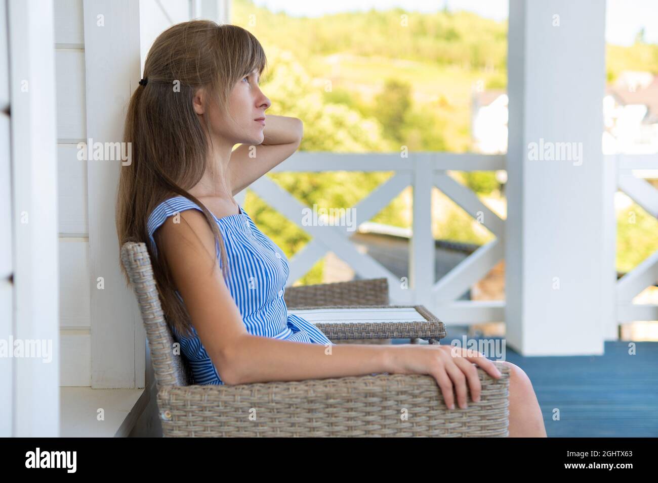 Side view of beautiful brunette woman in blue dress sitting on knitted ...