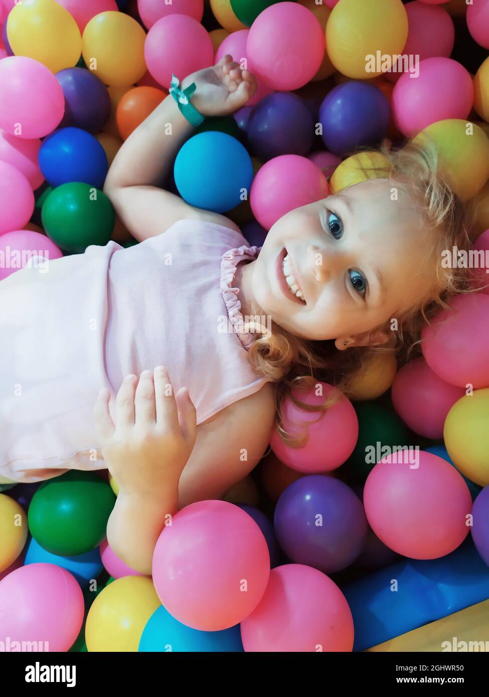 Overhead view of a smiling girl lying in a ball pit filled with multi ...