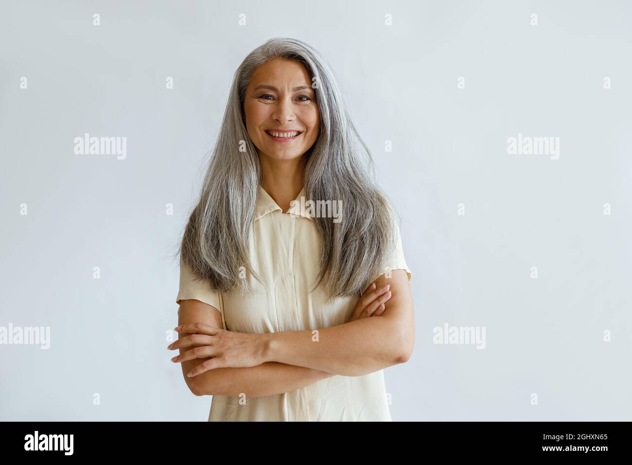 Portrait of smiling Asian woman with hoary hair and crossed arms on ...