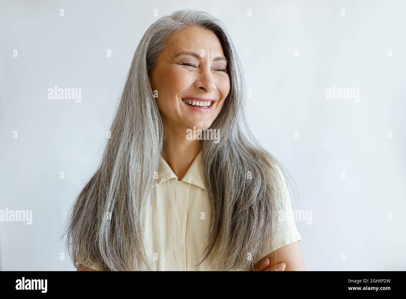 Portrait of smiling Asian woman with hoary hair and crossed arms on ...
