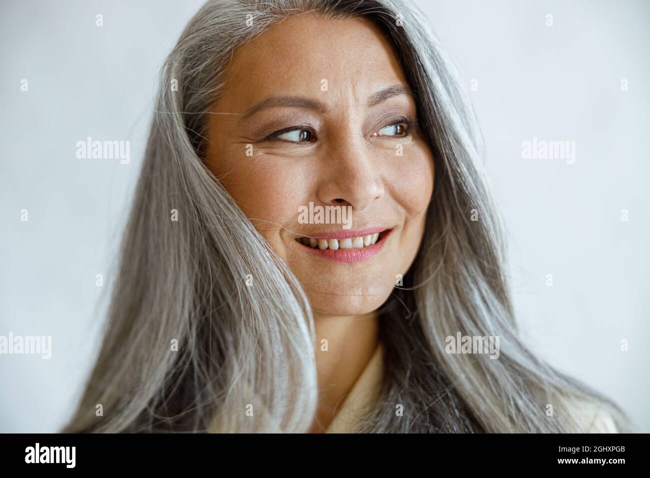 Asian lady with loose grey hair poses for camera on light background ...