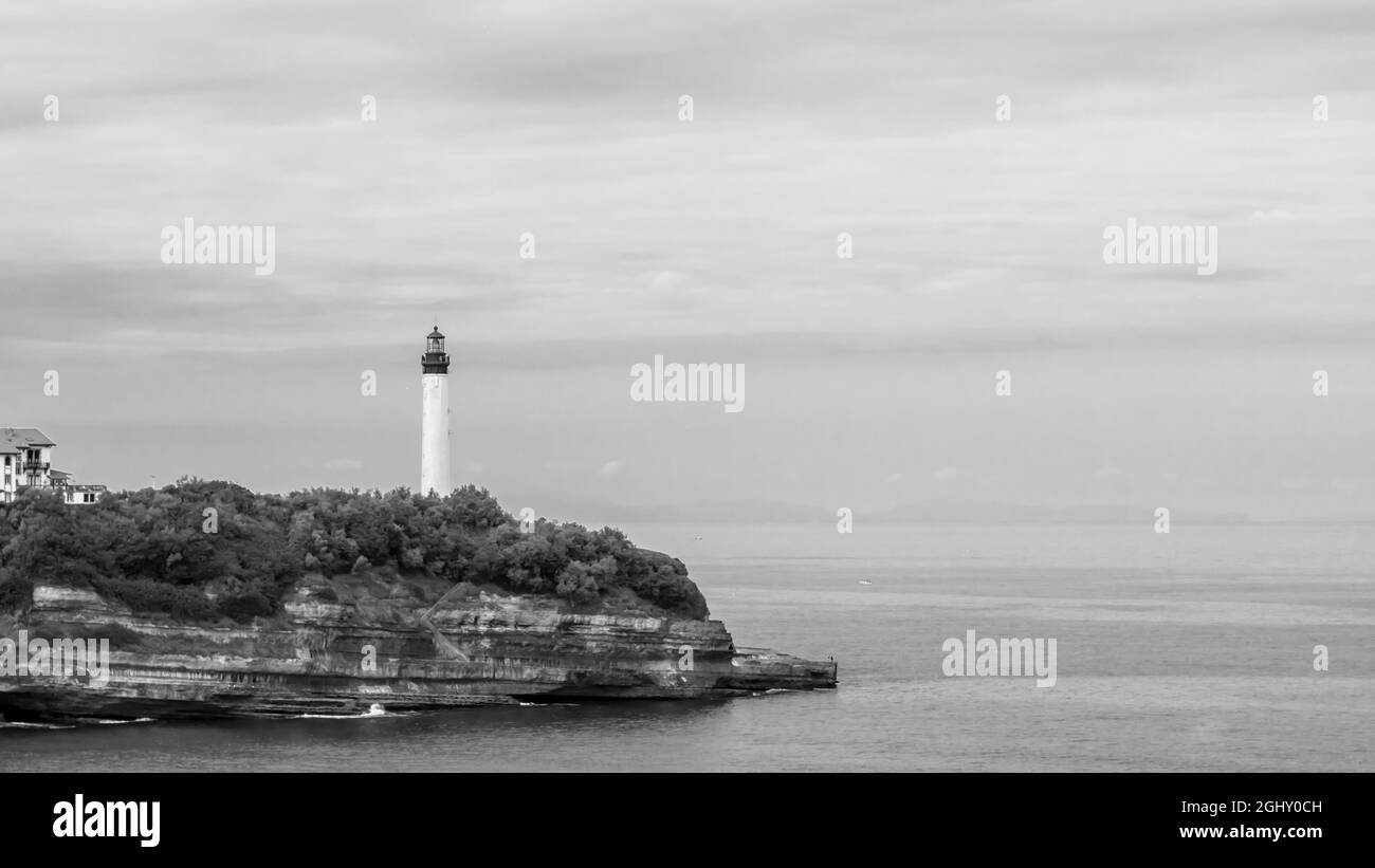 Grayscale shot of a landmark with a lighthouse with gray sea merging ...
